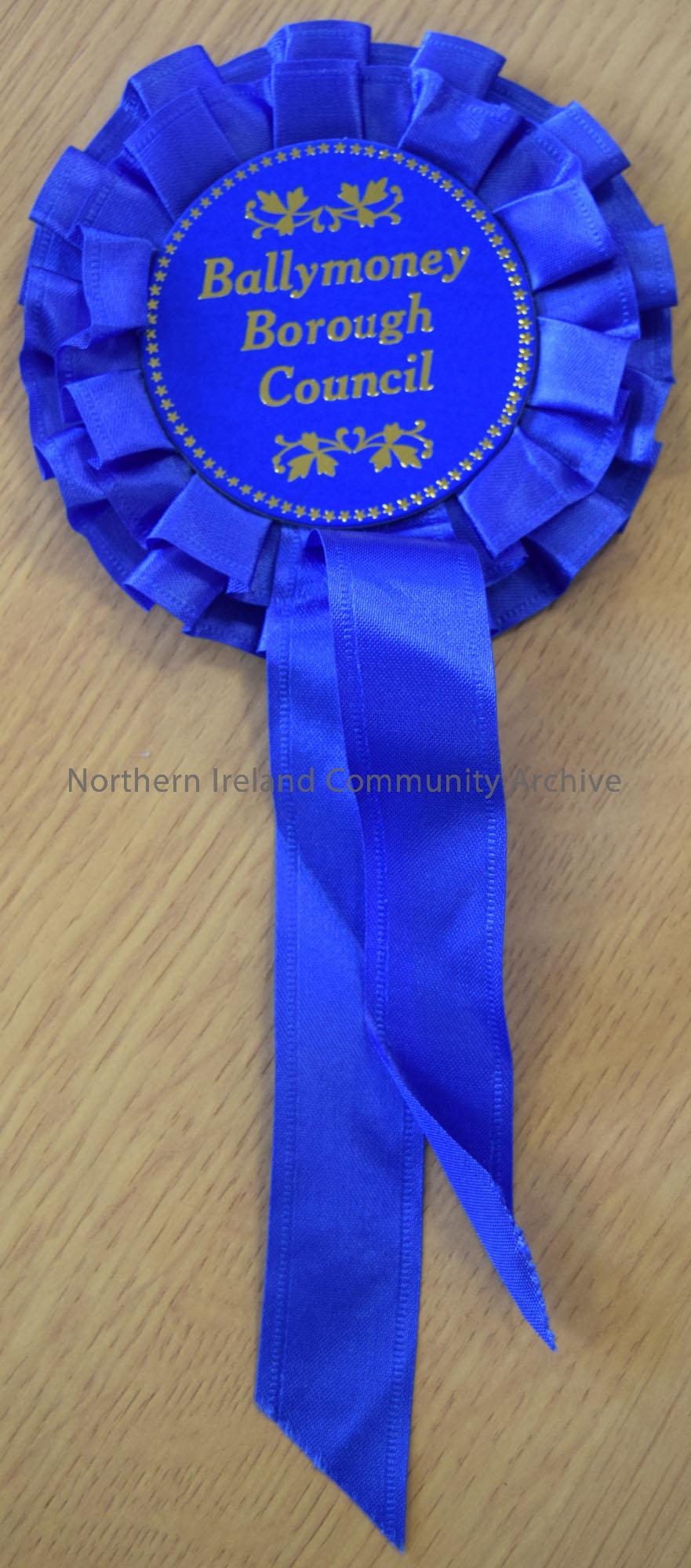 Blue rosette with two blue ribbons. On the face of the rosette in gold ...